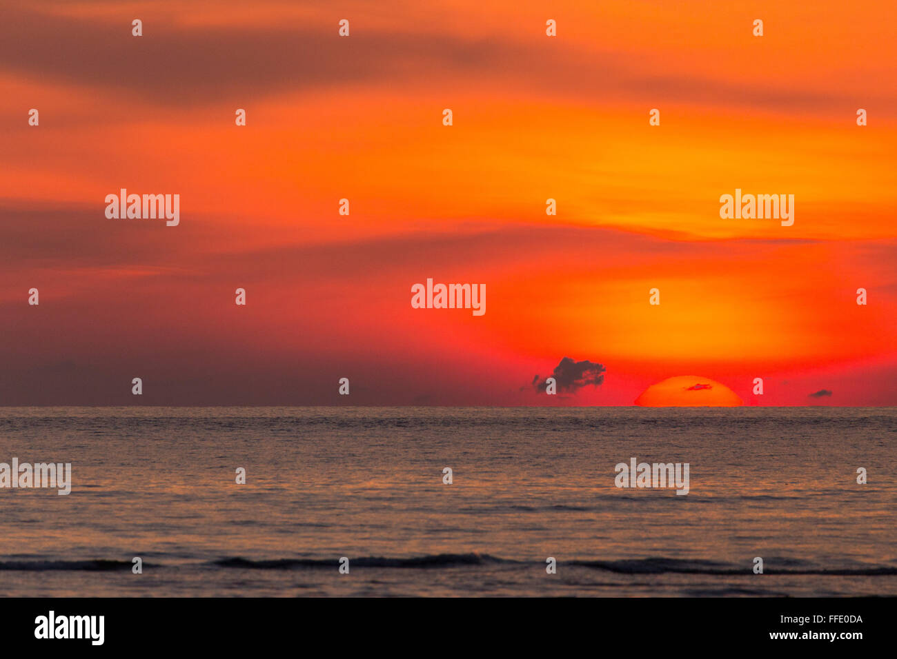 Deep red sunset as the sun sinks below the horizon off a beach in ...