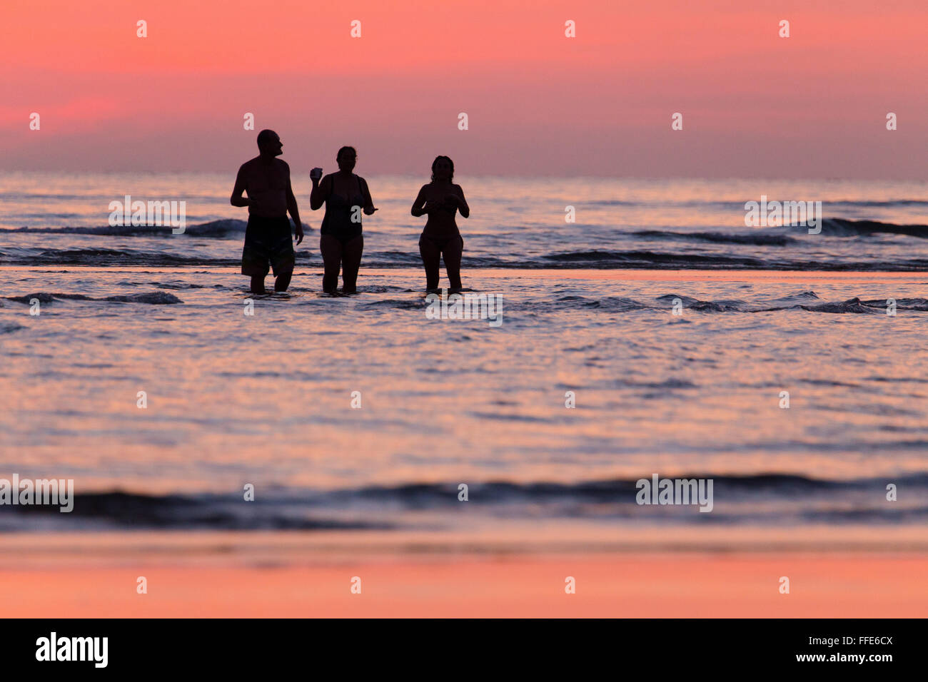 Three people standing in the sea at sunset off a beach in western Sabah ...