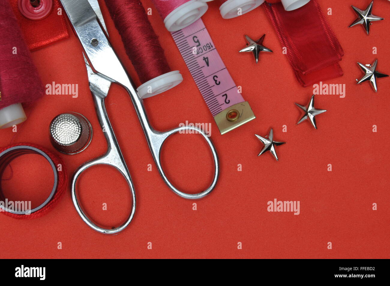 Sewing kit tool, scissors, thread and accessories on a red background ...
