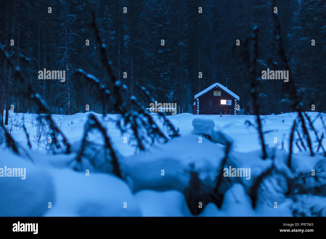 Cuthead Warden Cabin is lit up at dusk in the cold, snowy forests of ...