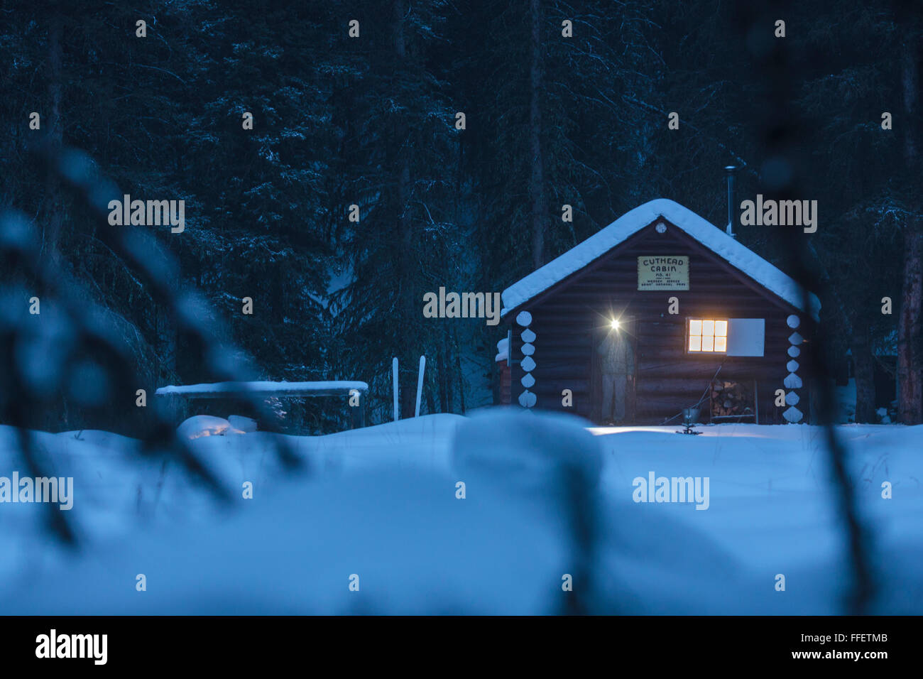 Cuthead Warden Cabin is lit up at dusk in the cold, snowy forests of ...