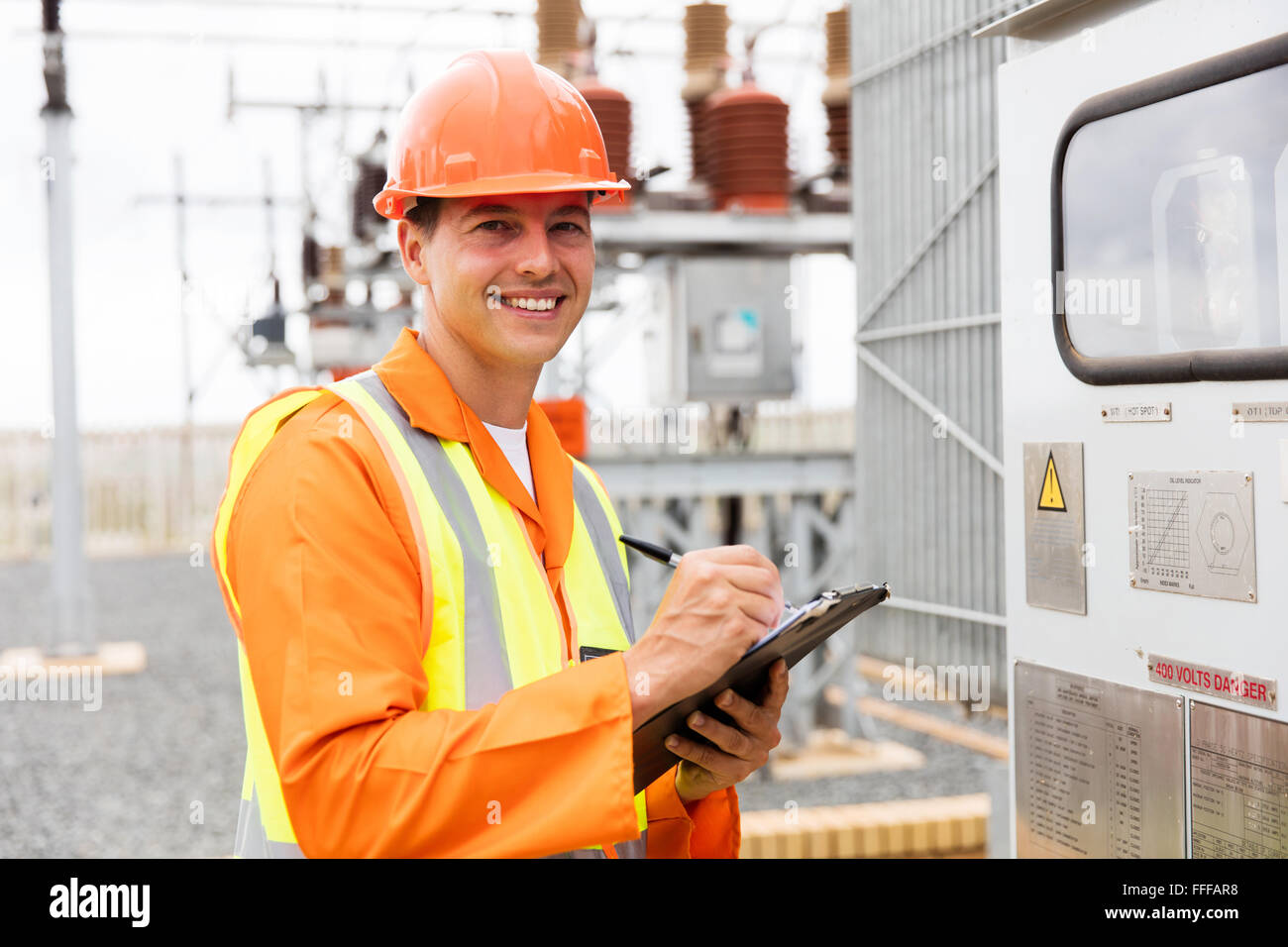 portrait of happy young electric worker taking transformer readings ...