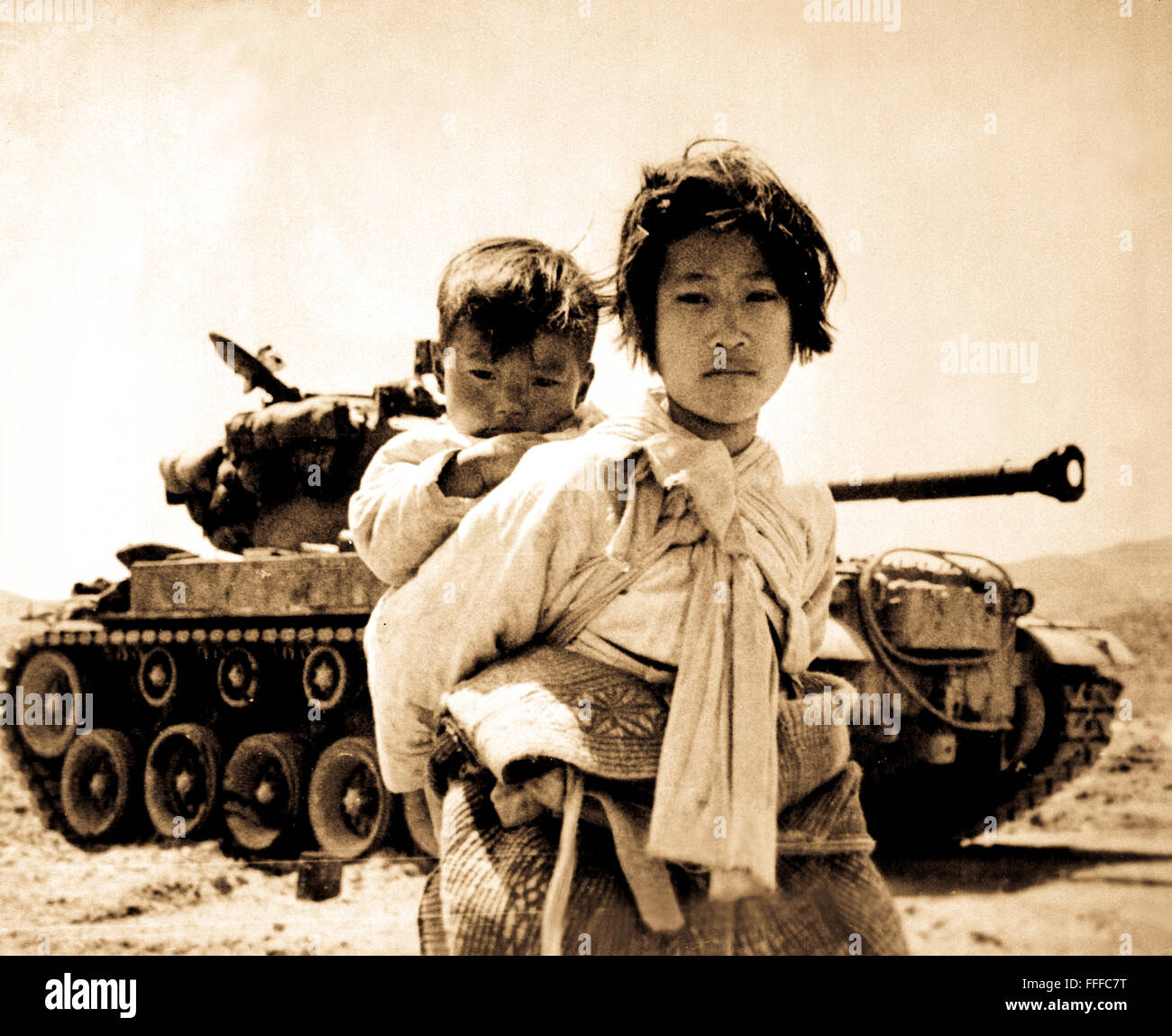 With her brother on her back a war weary Korean girl tiredly trudges by ...