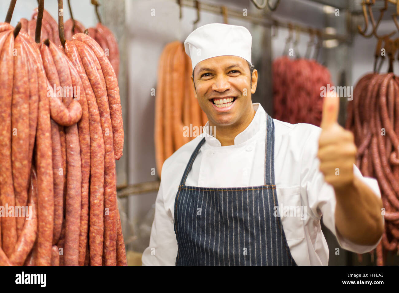 cheerful middle aged butcher giving thumb up against wors hanging in ...