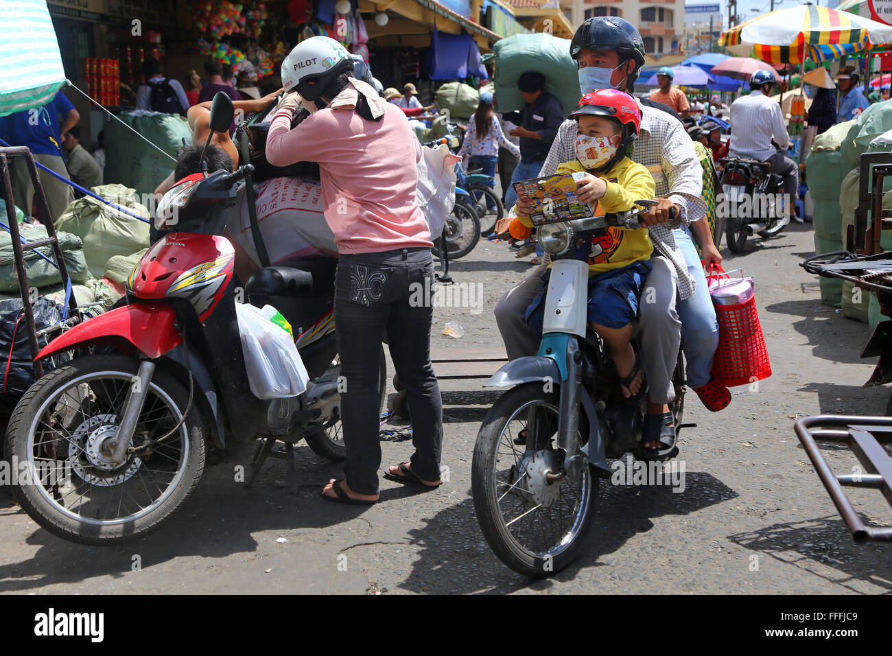 A young boy rides on the front of his father's moped through a market ...