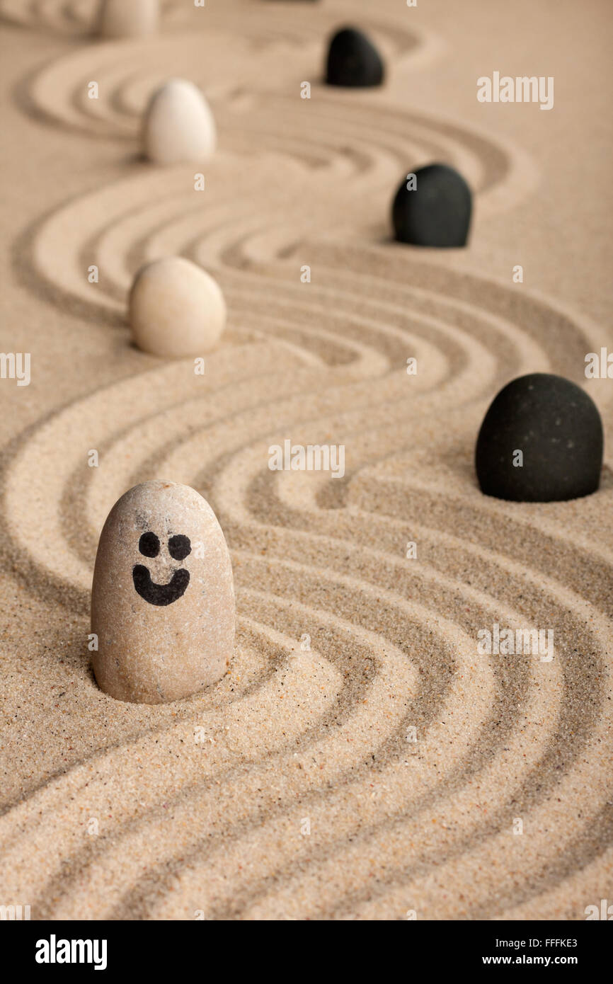 Stone smiley sticking out of the sand, between white and black stones ...