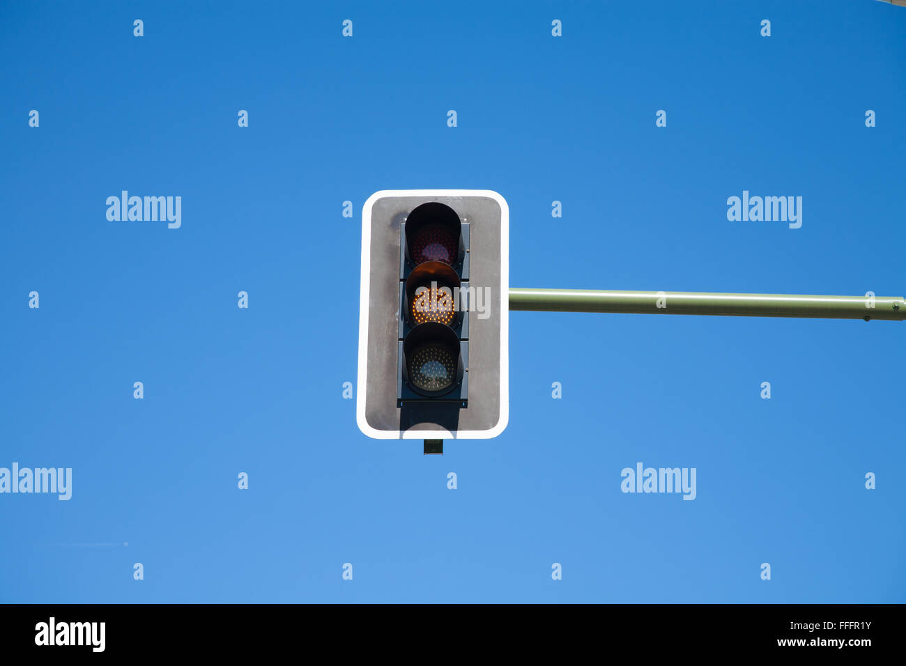 traffic light semaphore orange light on green and red lights off in green pole on blue sky ...