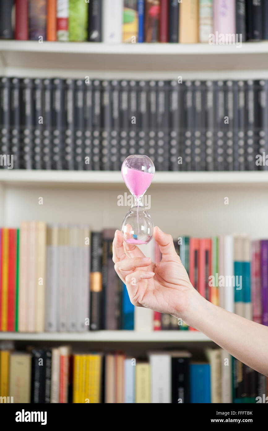 pink sand clock in woman hand over library background Stock Photo - Alamy