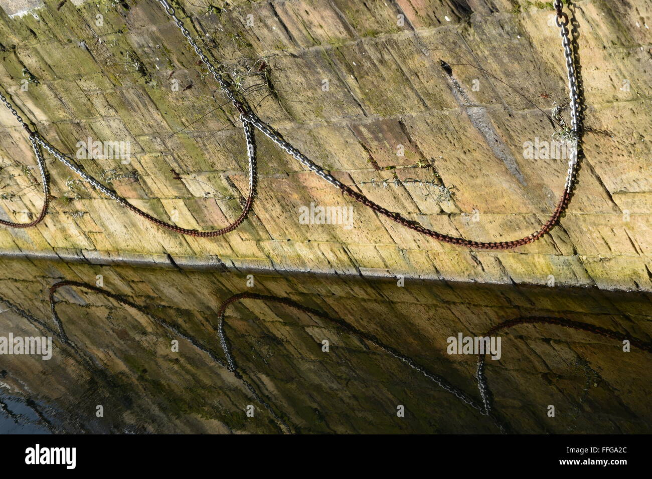 Dock wall with chains reflected in the water Stock Photo - Alamy
