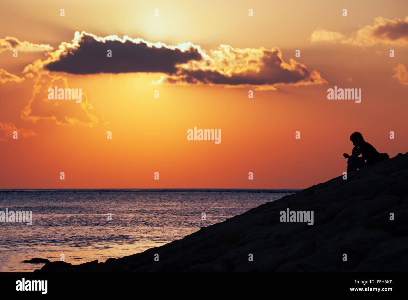 Black silhouette of thinking man sitting alone on the sea beach reading ...