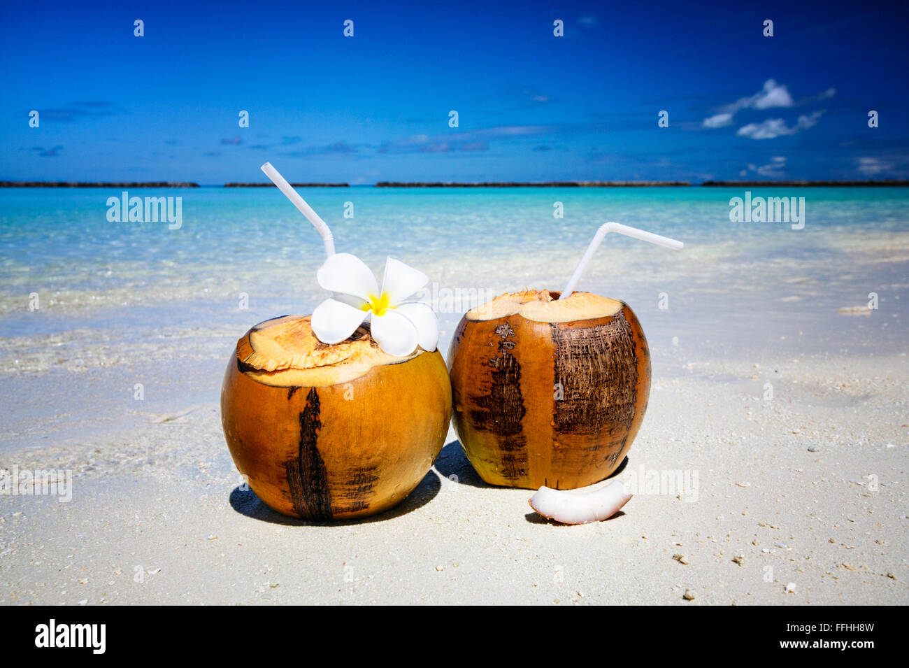 Two coconut cocktails on white sand beach next to clean sea blue water ...