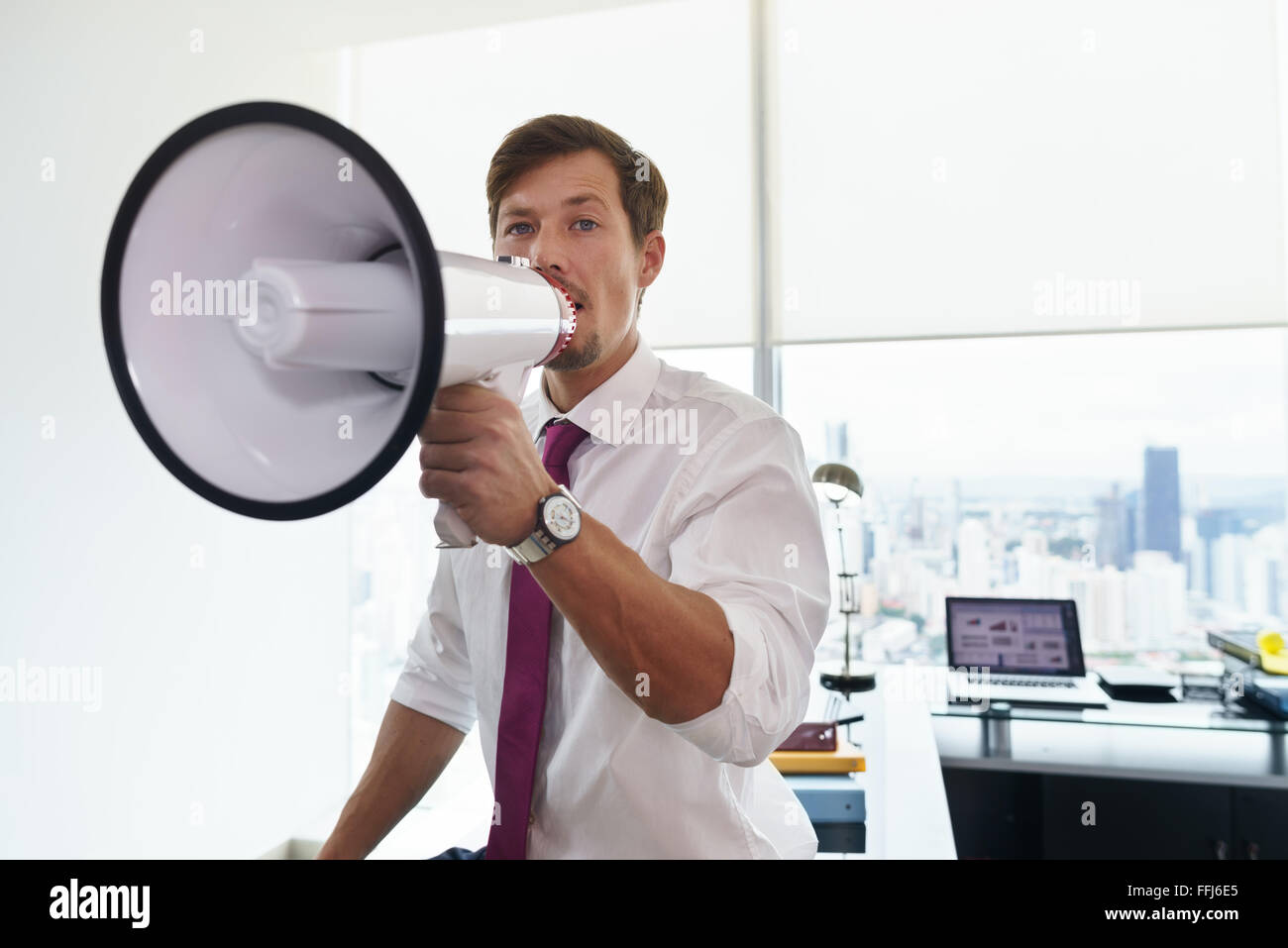 Young executive office worker holding megaphone and speaking at camera ...