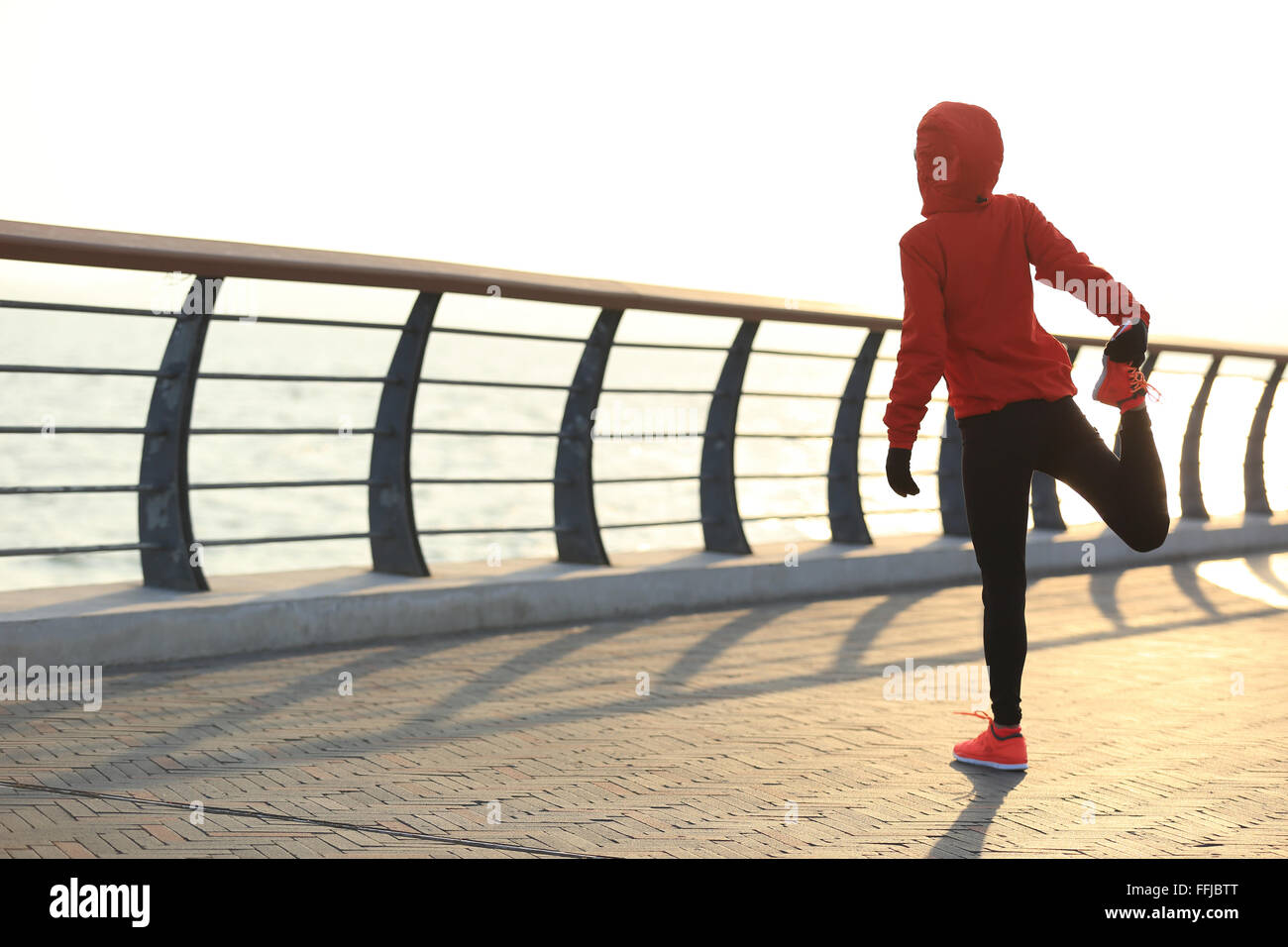 Young female runner stretching her legs on sunrise seaside Stock Photo ...