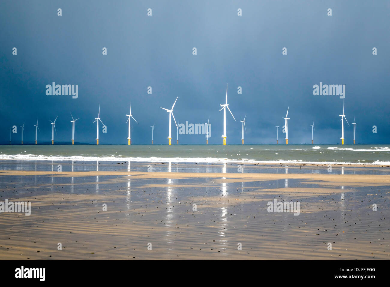 Sun lit Redcar Wind Farm from the beach with dark storm clouds behind ...