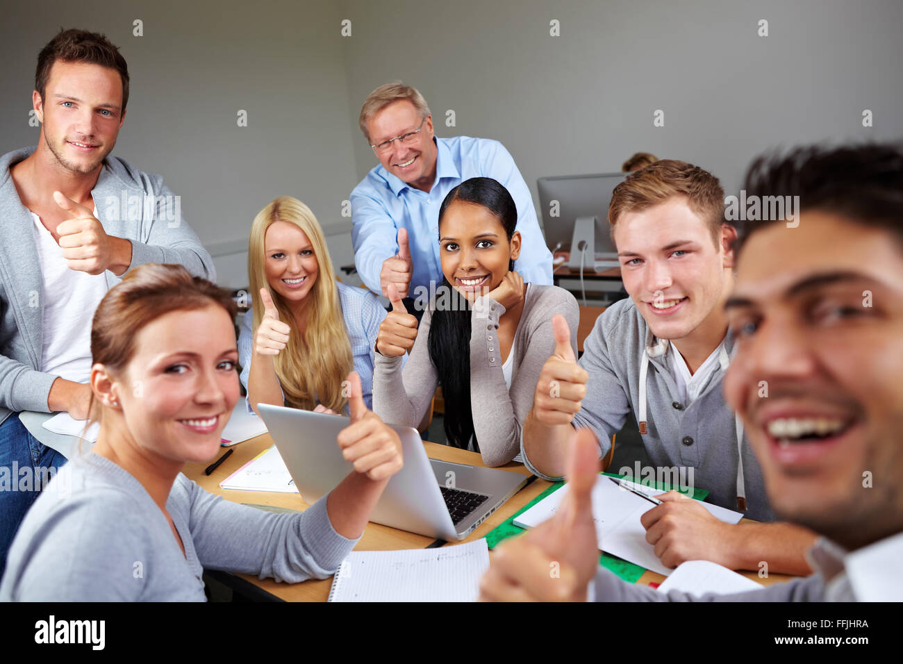 Happy students holding thumbs up in university Stock Photo - Alamy