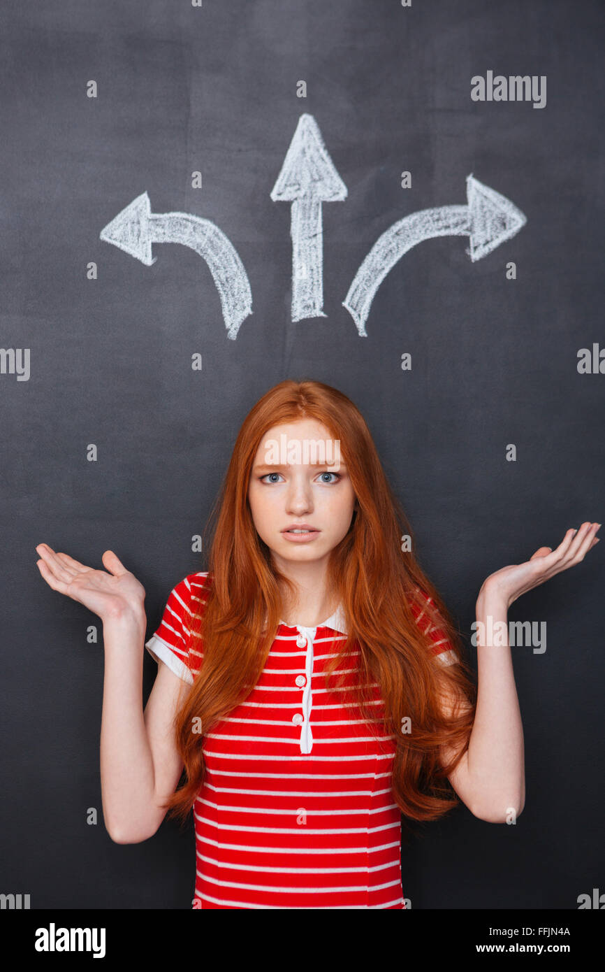Sad confused young woman choosing direction over blackboard background ...