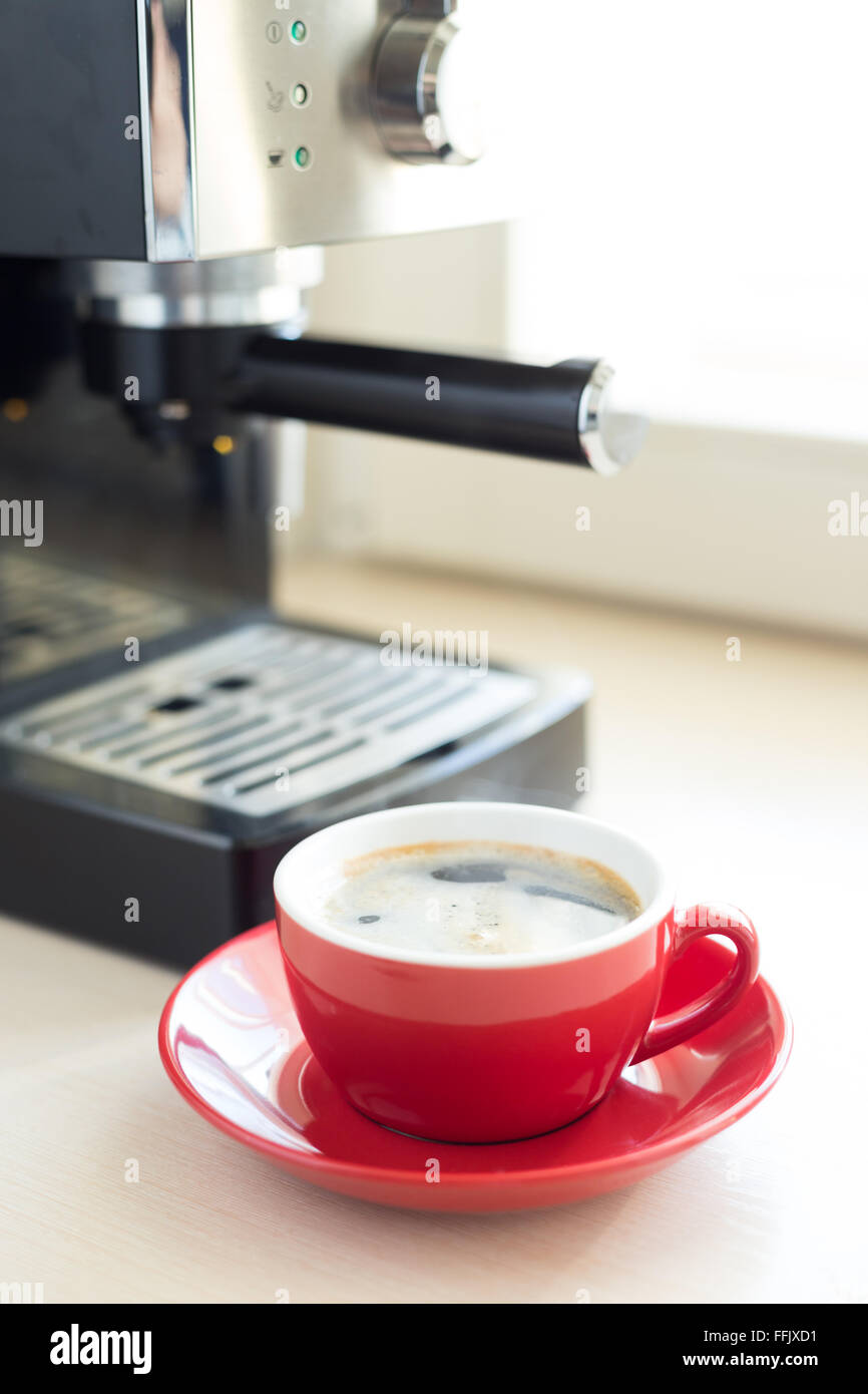 Red cup of coffee with coffee machine behind. Brewing morning coffee or ...