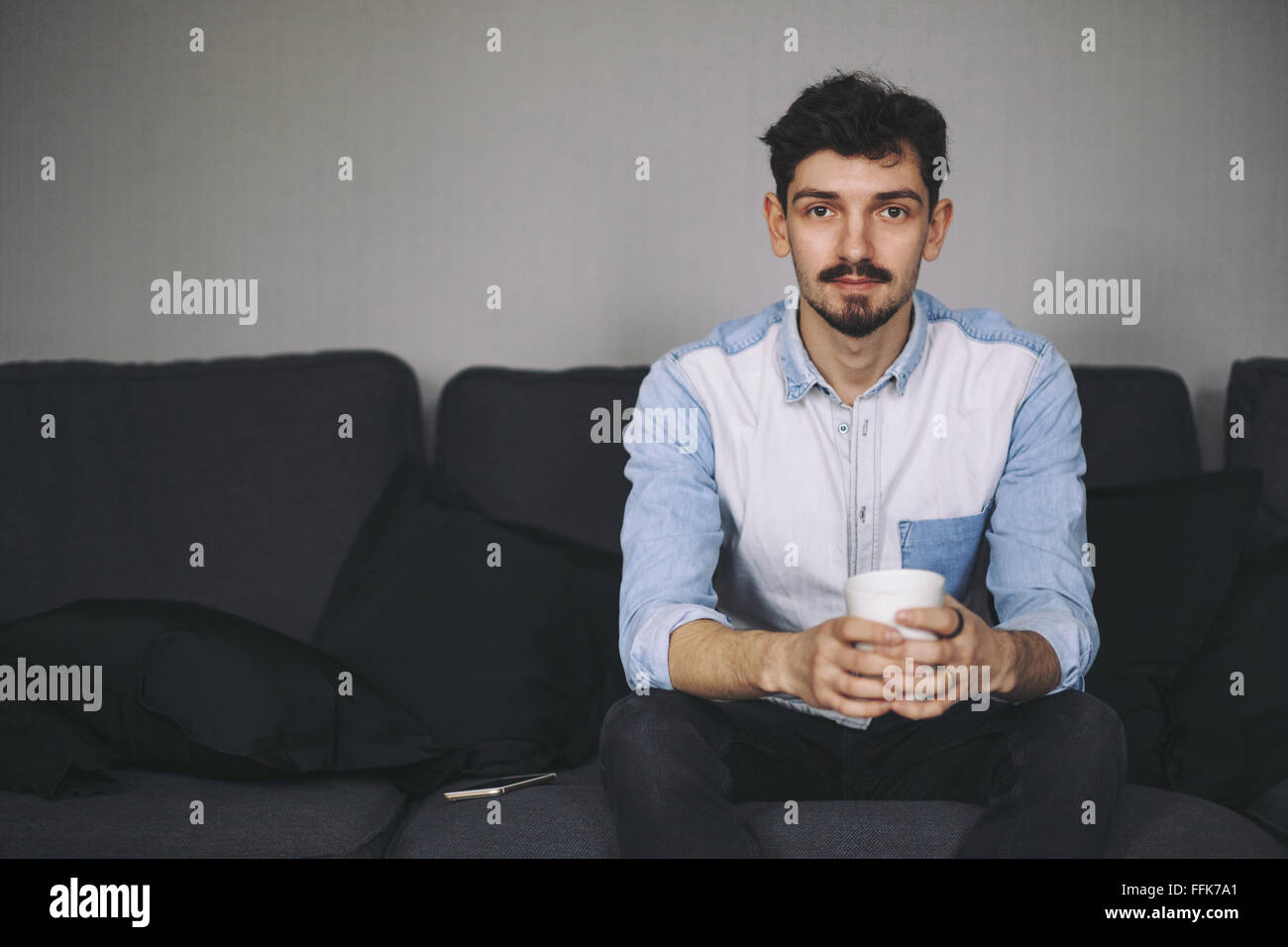 Handsome casual man sitting on couch having coffee Stock Photo - Alamy