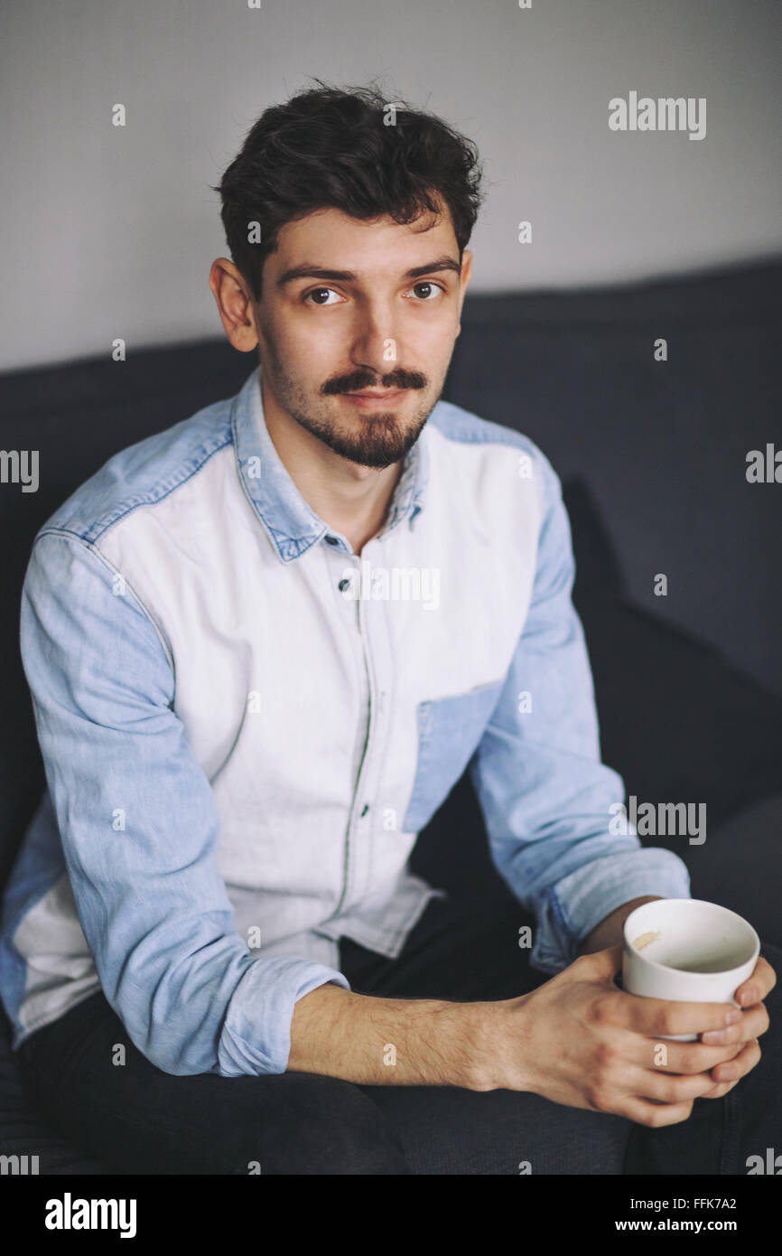 Handsome casual man sitting on couch having coffee Stock Photo - Alamy