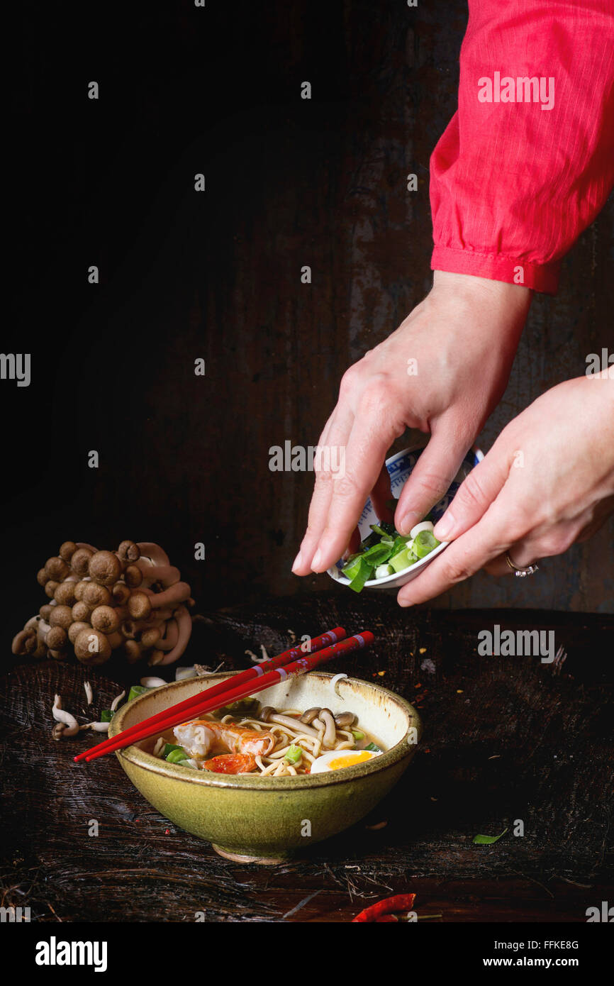 Female hand in red shirt sprinkle with sliced spring onion asian ramen ...