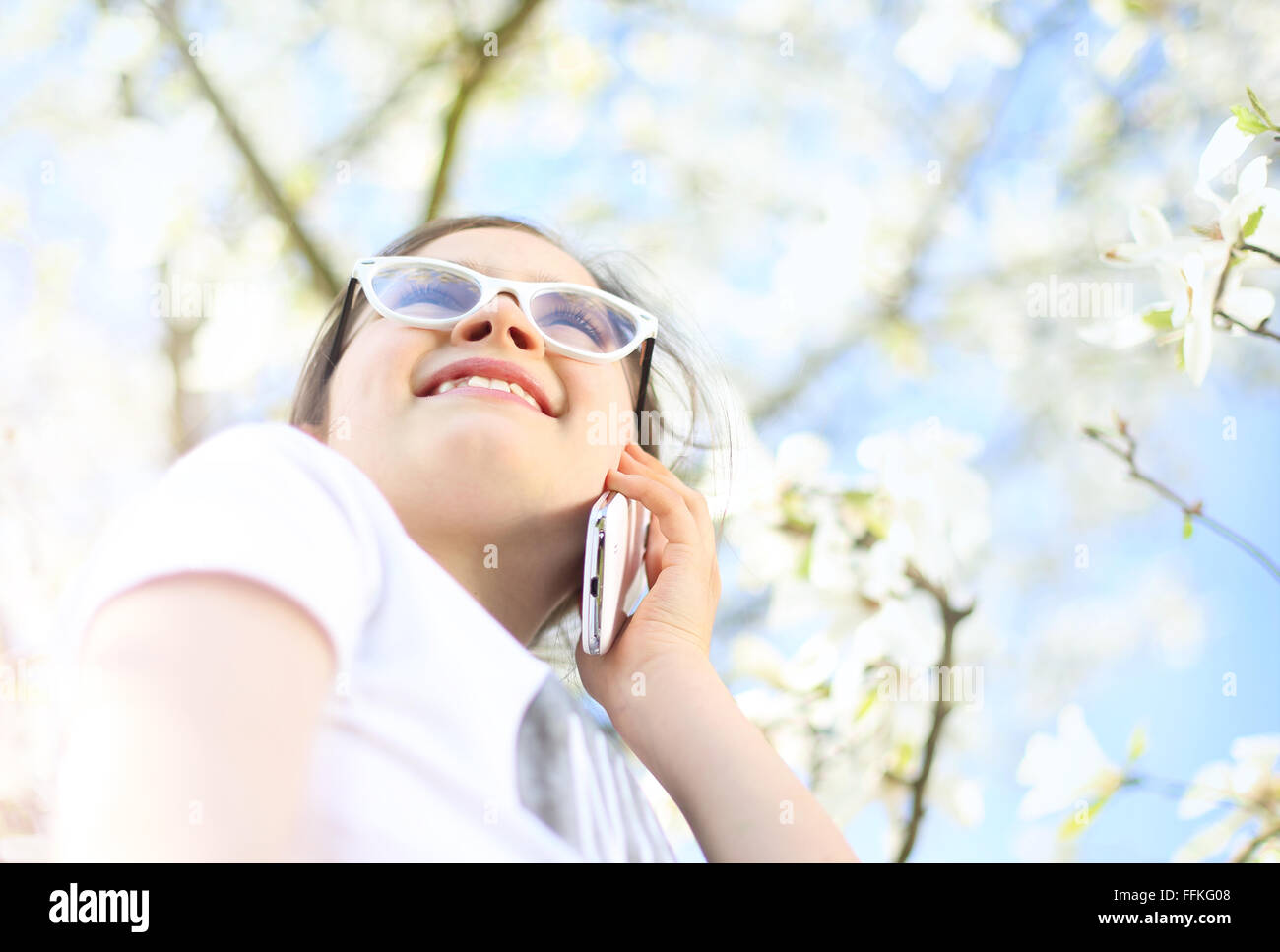 A girl talking on a cell phone while standing under a tree flowered ...