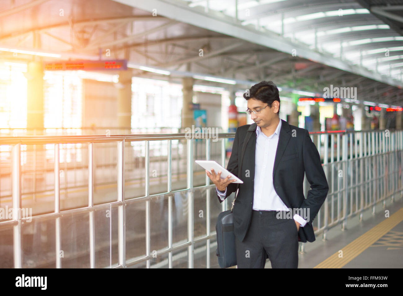 indian business male using tablet computer while waiting for train ...