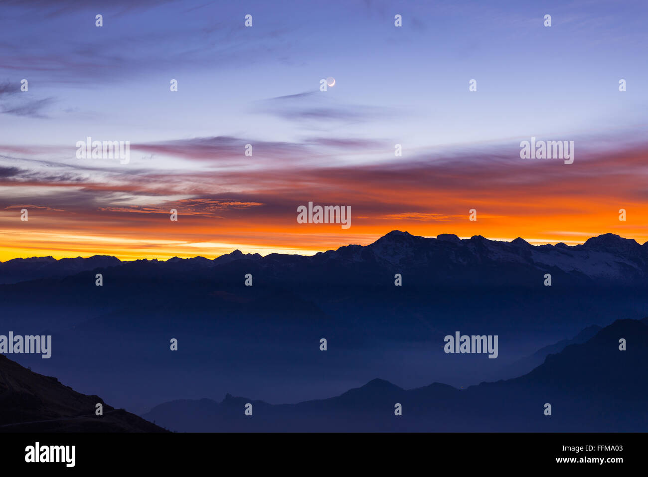 Colorful sunset behind majestic mountain peaks of the Italian Alps. Fog ...