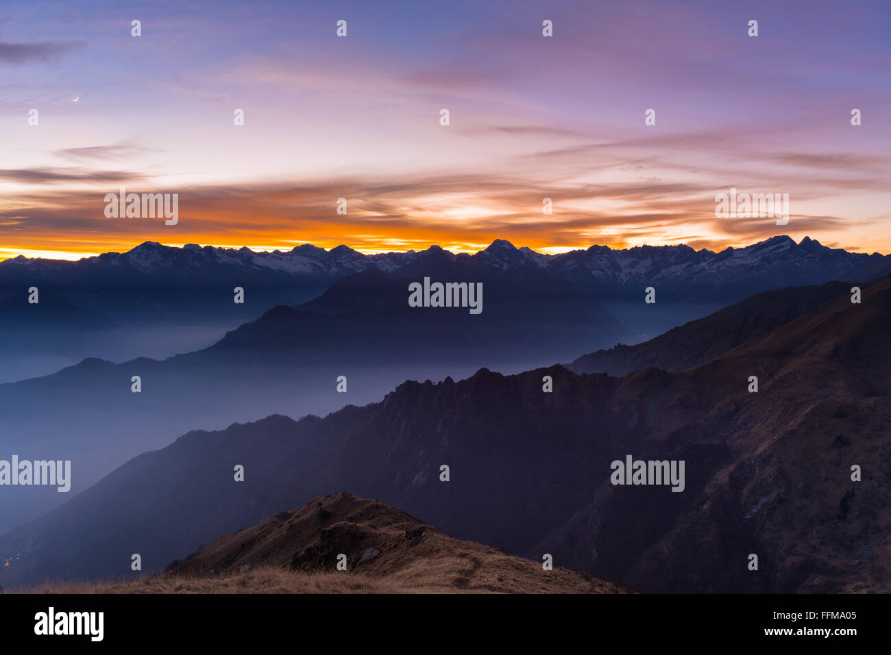 Colorful sunset behind majestic mountain peaks of the Italian Alps. Fog ...