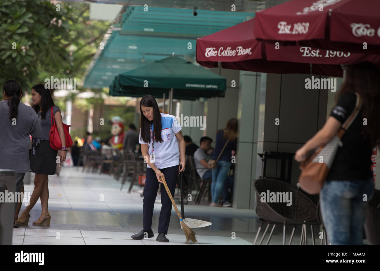 A young woman sweeping the sidewalk with a brush in Cebu City ...