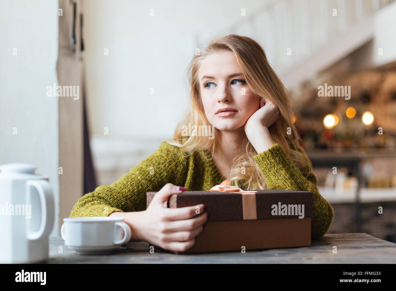 Woman sitting at the table with gift box and waiting for somebody Stock ...