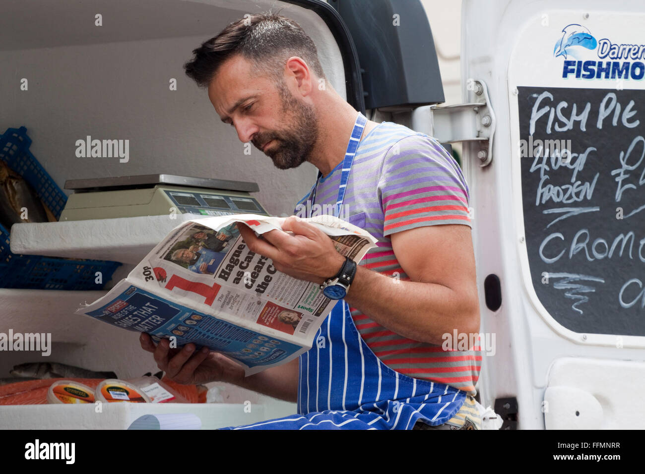 Mobile fishmonger in a traditional striped apron reads the newspaper ...