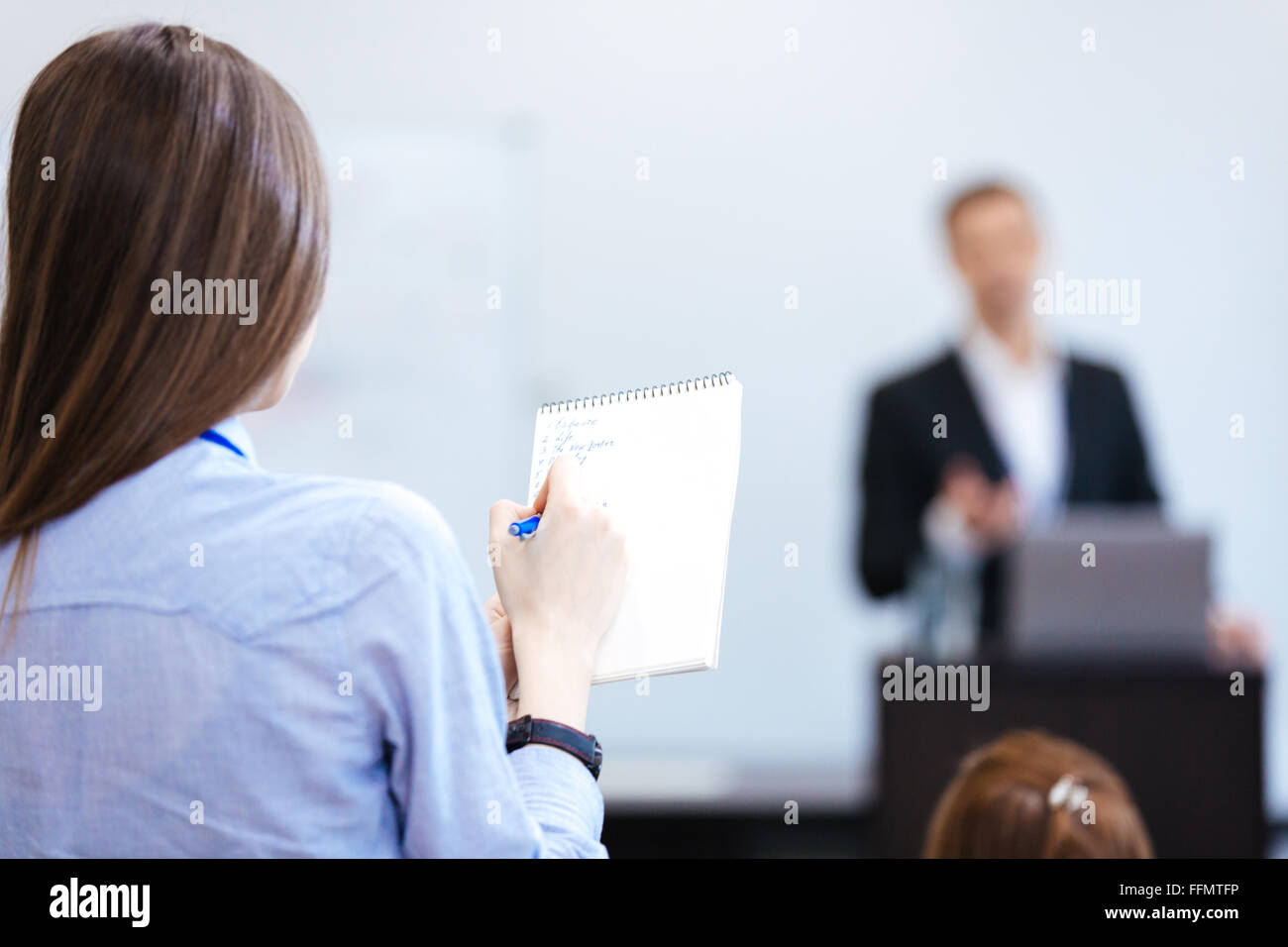 Back view of young business woman writing and making notes in notepad ...