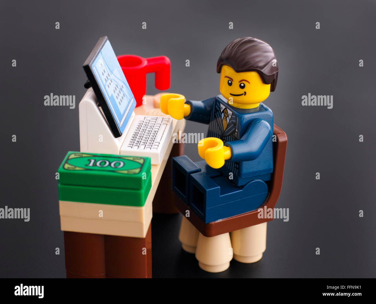 Lego businessman sits at his working table with computer, money and cup ...