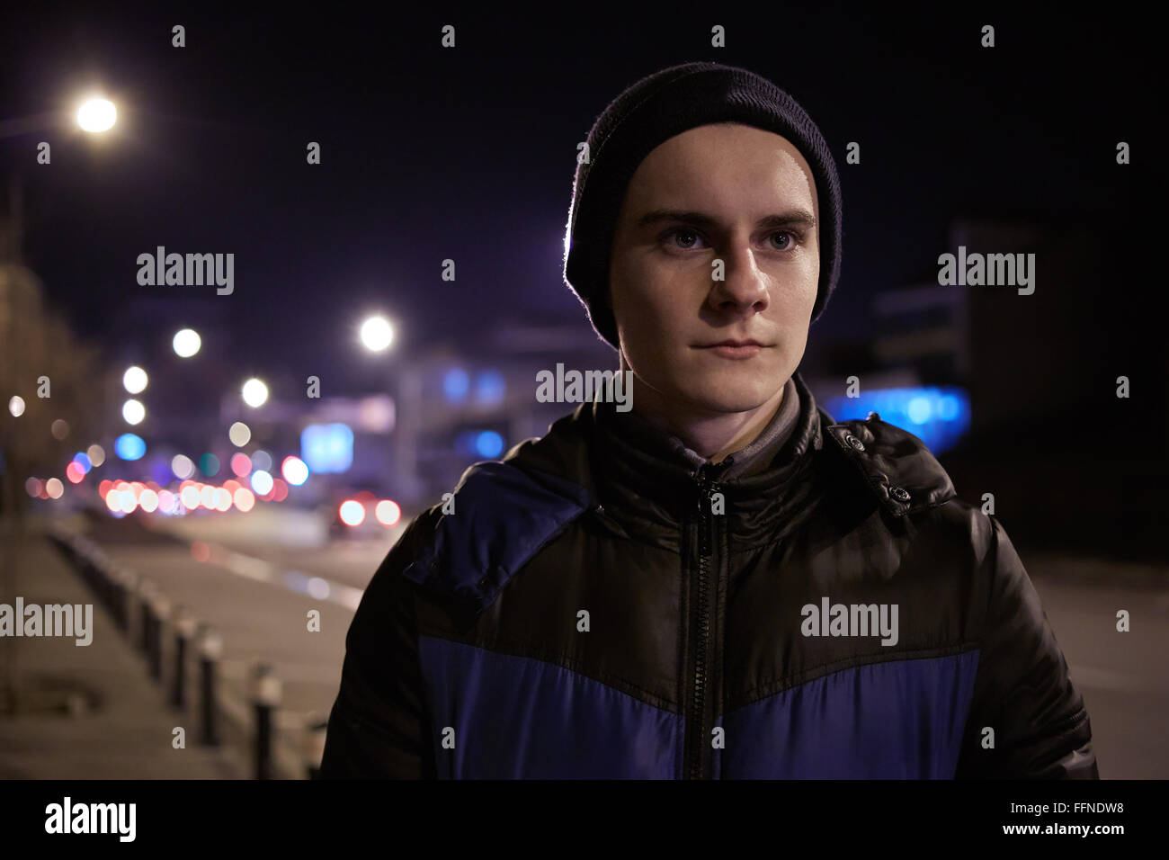 Closeup of a teenage boy at night with city lights in blurred ...