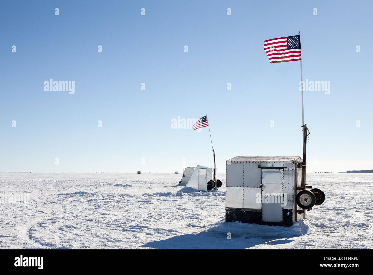 Ice shanties on a frozen lake flying American flags. Backlighting ...