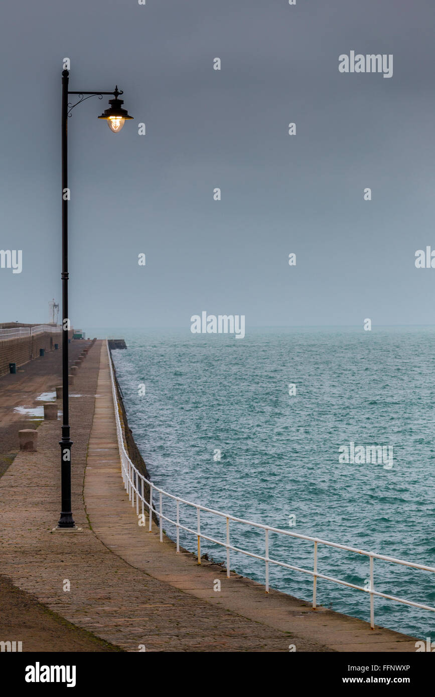 A lamp post light on a pier on a gloomy day with the sea in the ...