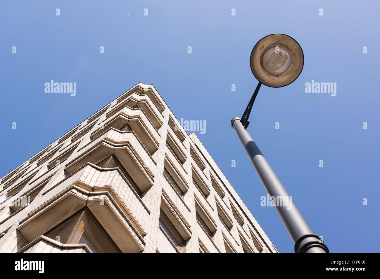 View from below of a street lamp with block of flats and blue sky in ...