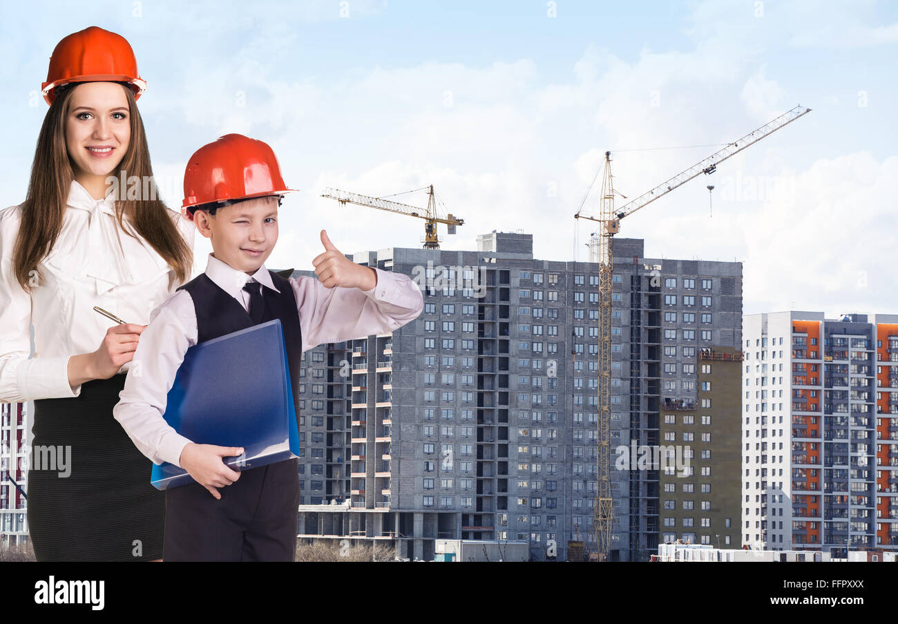 Young little builder boy in the orange helmet stands on the buildings ...