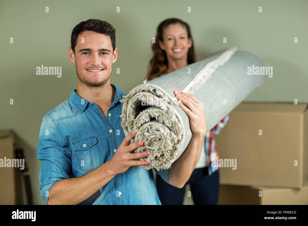 Happy couple carrying rolled up rug Stock Photo - Alamy