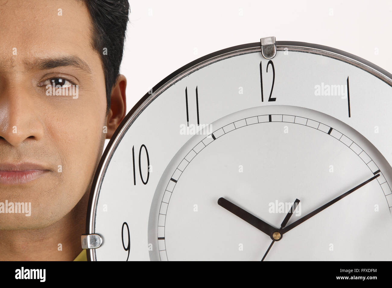 Businessman holding wall clock in one hand next his left side of face ...