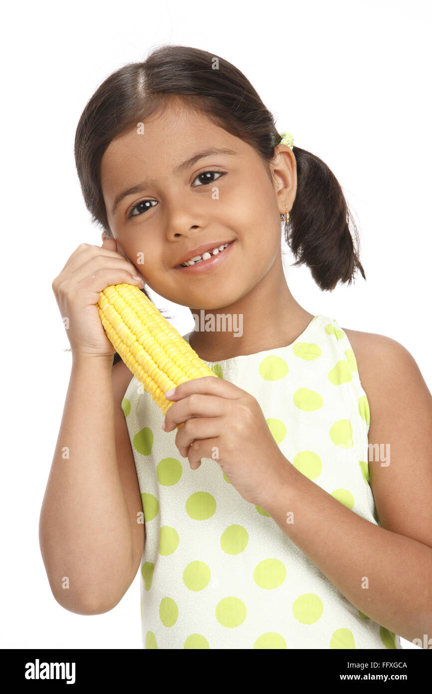 Eight year old girl holding sweet corn in both hands near her cheek MR ...