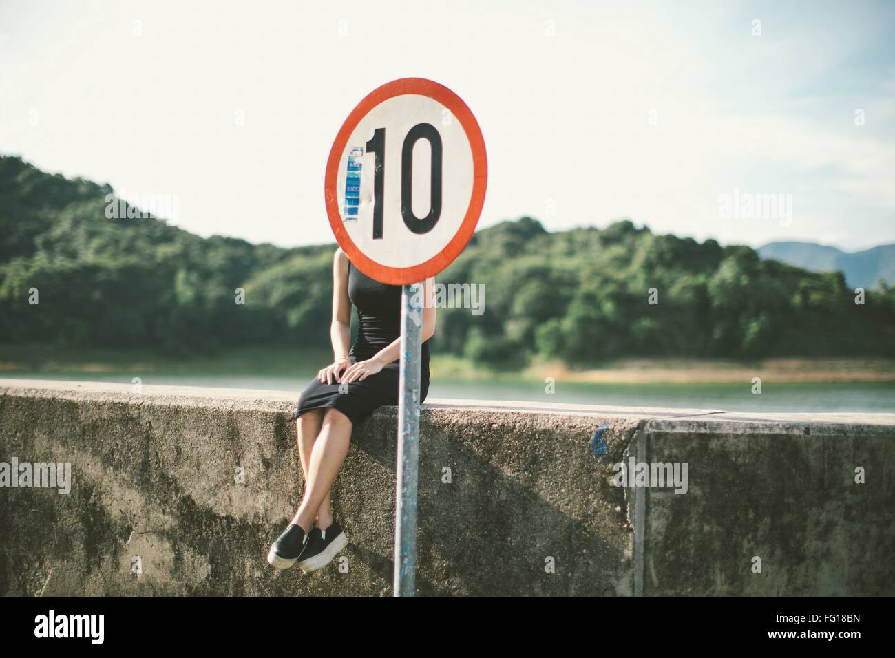 Woman sitting on retaining wall behind speed limit signboard Stock ...