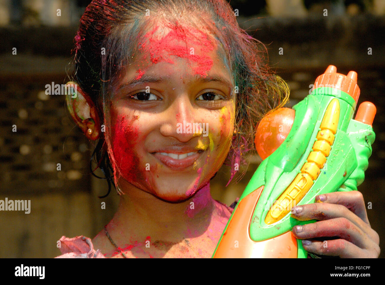Coloured face of girl holding syringe pichkari enjoying holi festival ...