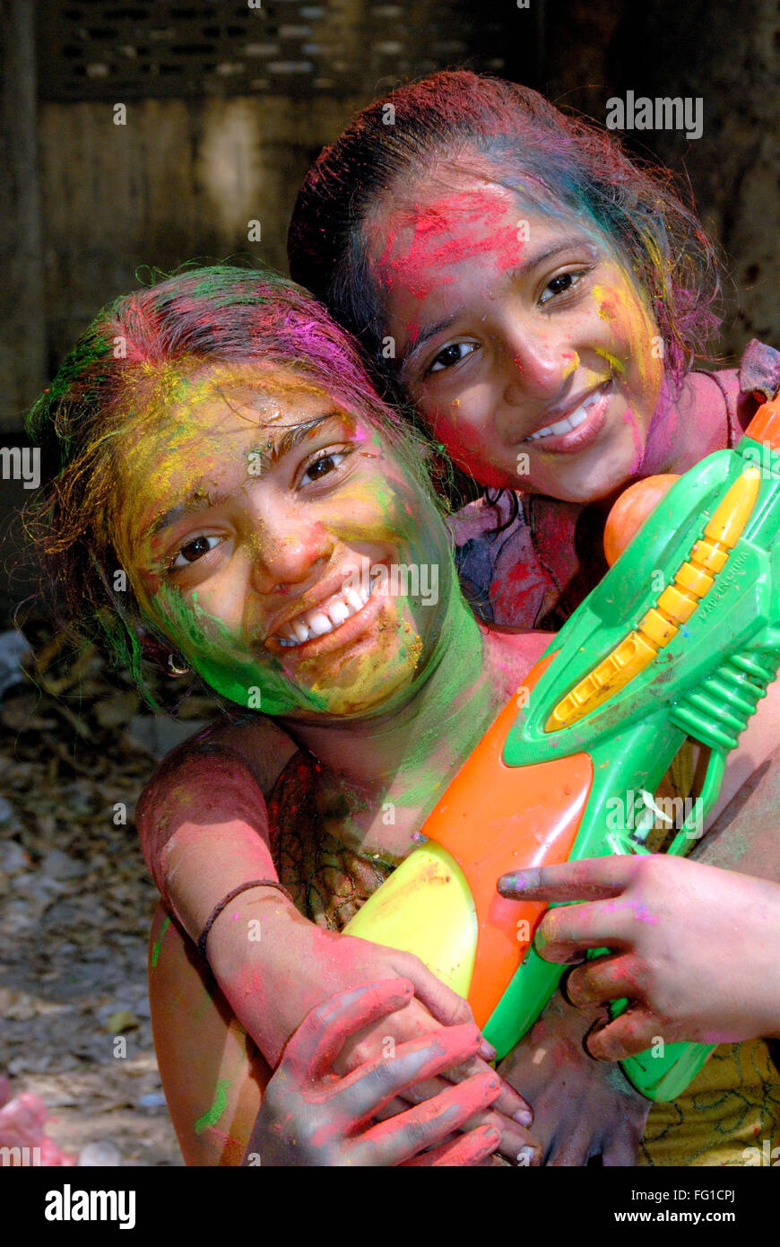 Coloured faces of young girls holding syringe pichkari enjoying holi ...