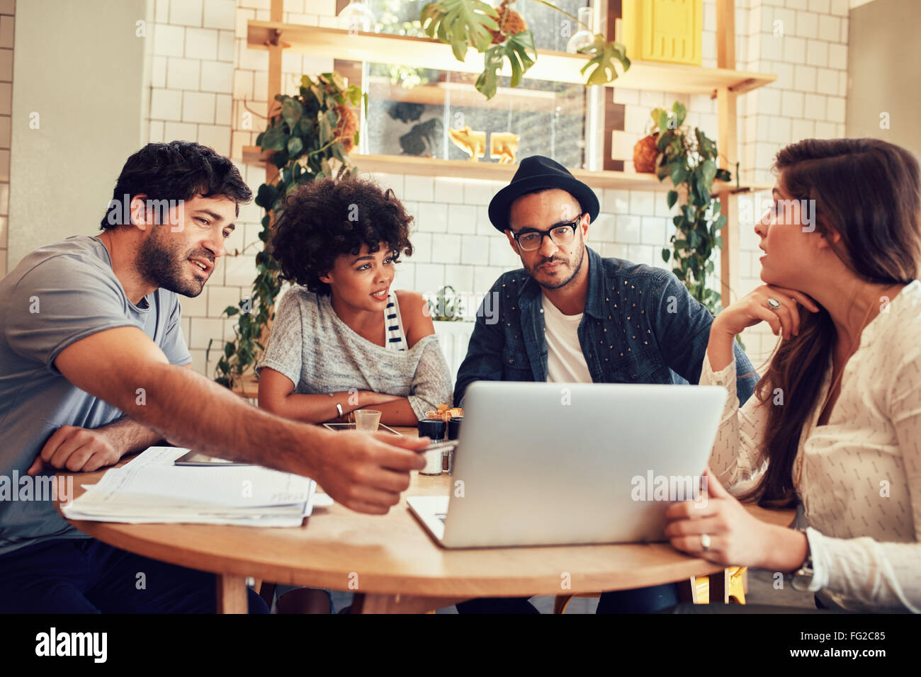 Portrait of young people sitting around a table in cafe with a laptop ...