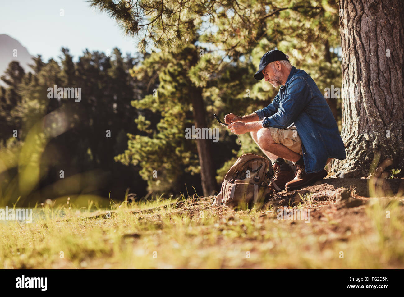 Portrait of senior hiker checking his compass. Mature man sitting by a ...