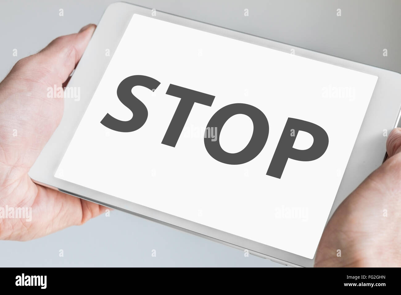 Stop text displayed on touch screen of modern tablet. Hands holding ...
