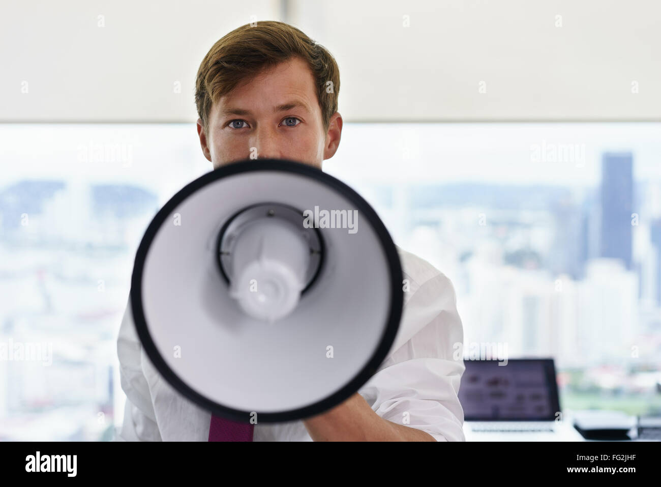 Young executive office worker holding megaphone and speaking at camera ...