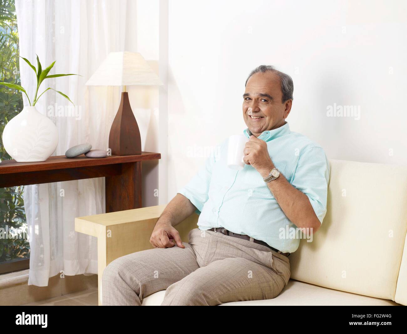 Old man showing white mug sitting on sofa MR#702T Stock Photo - Alamy