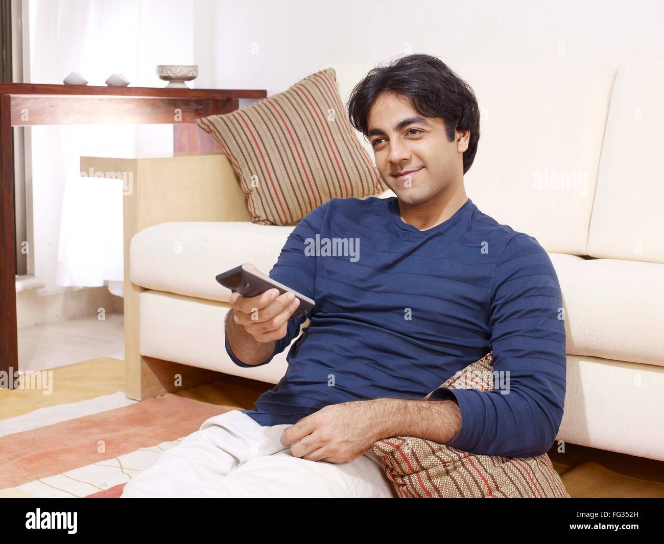 Young man holding remote control watching TV MR#702V Stock Photo - Alamy